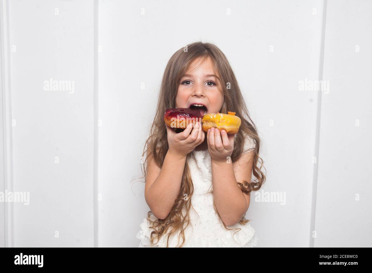 Little happy cute preschool girl is eating colourful donuts on white ...
