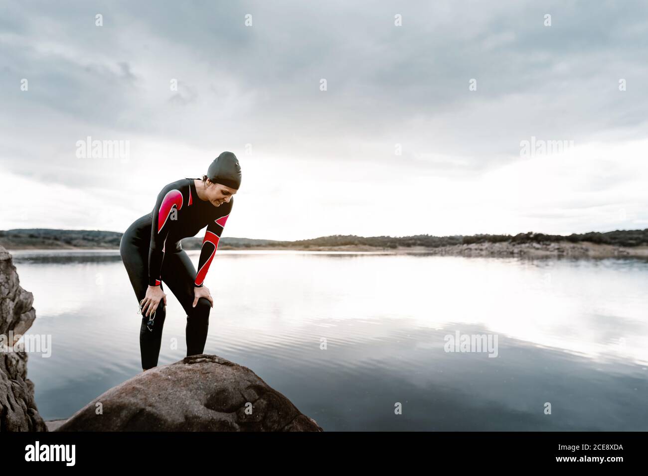 Side view slim tired female in black wetsuit standing resting on ...