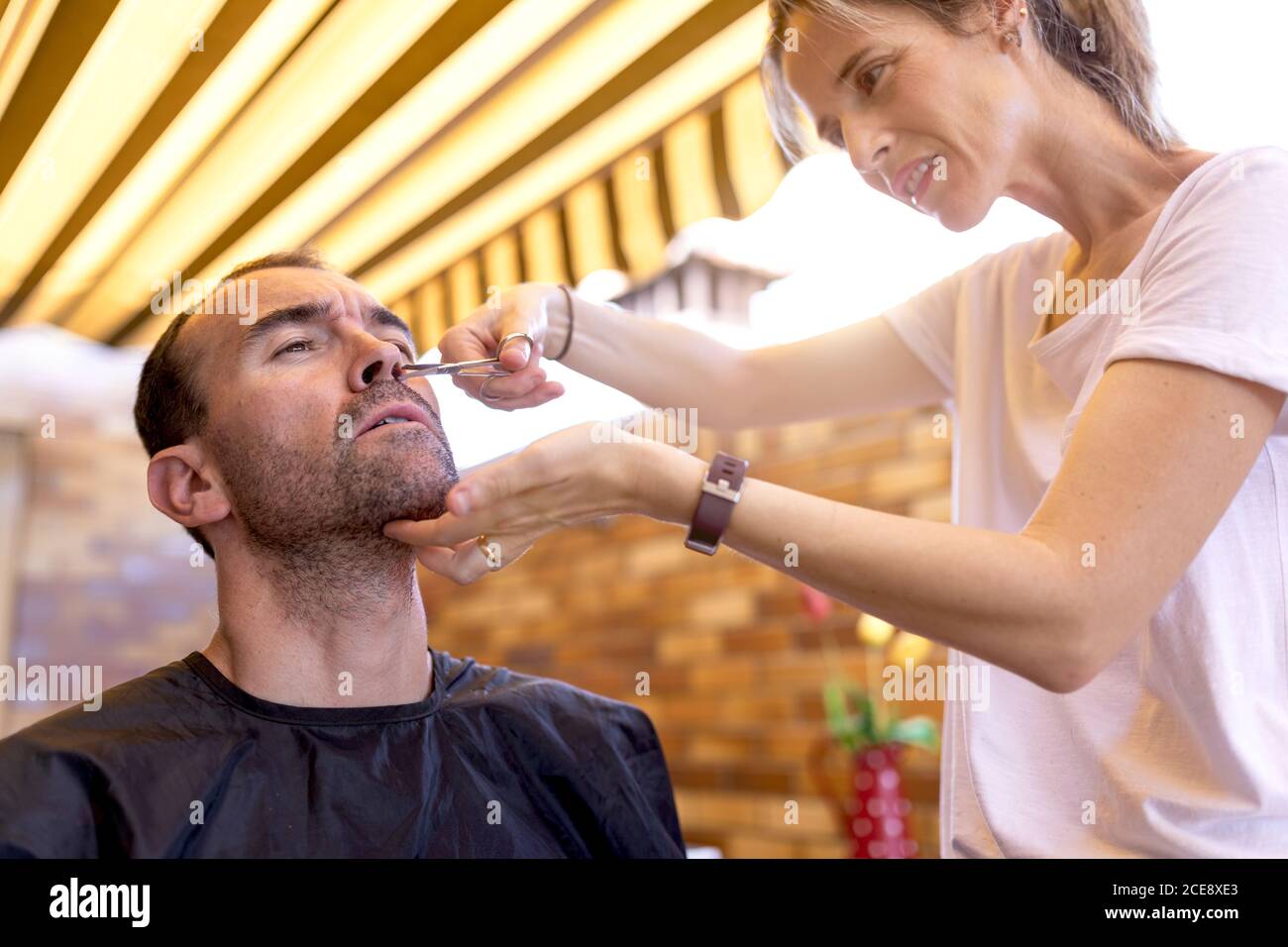 Female stylist in wristwatch trimming nose hair to bearded male client ...
