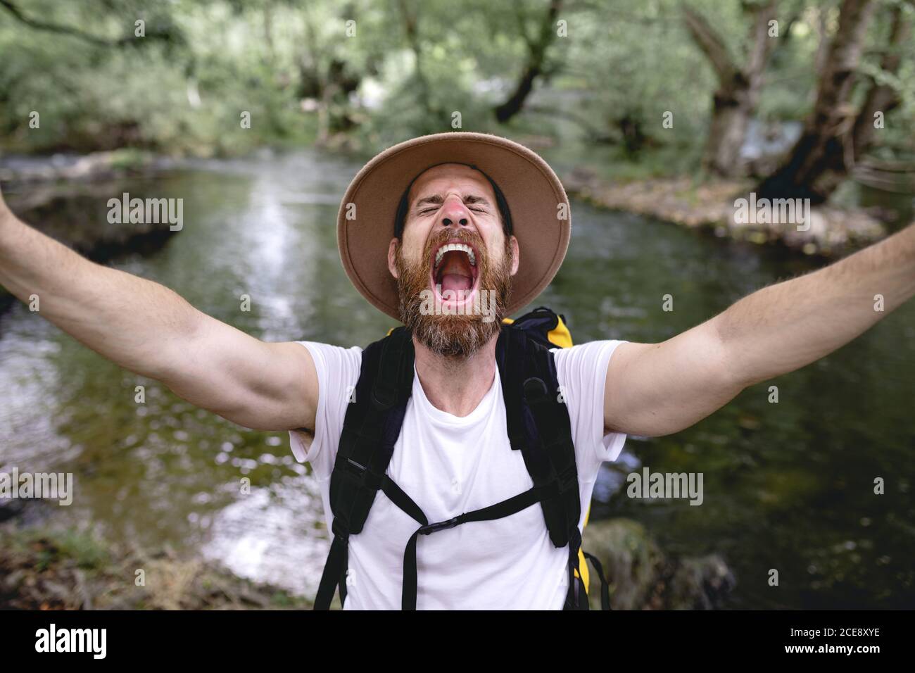 young man with beard hat on his head and yellow backpack hiking down a ...