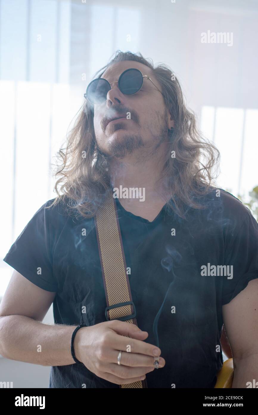 Shallow focus shot of a middle-aged male guitarist smoking in the room ...