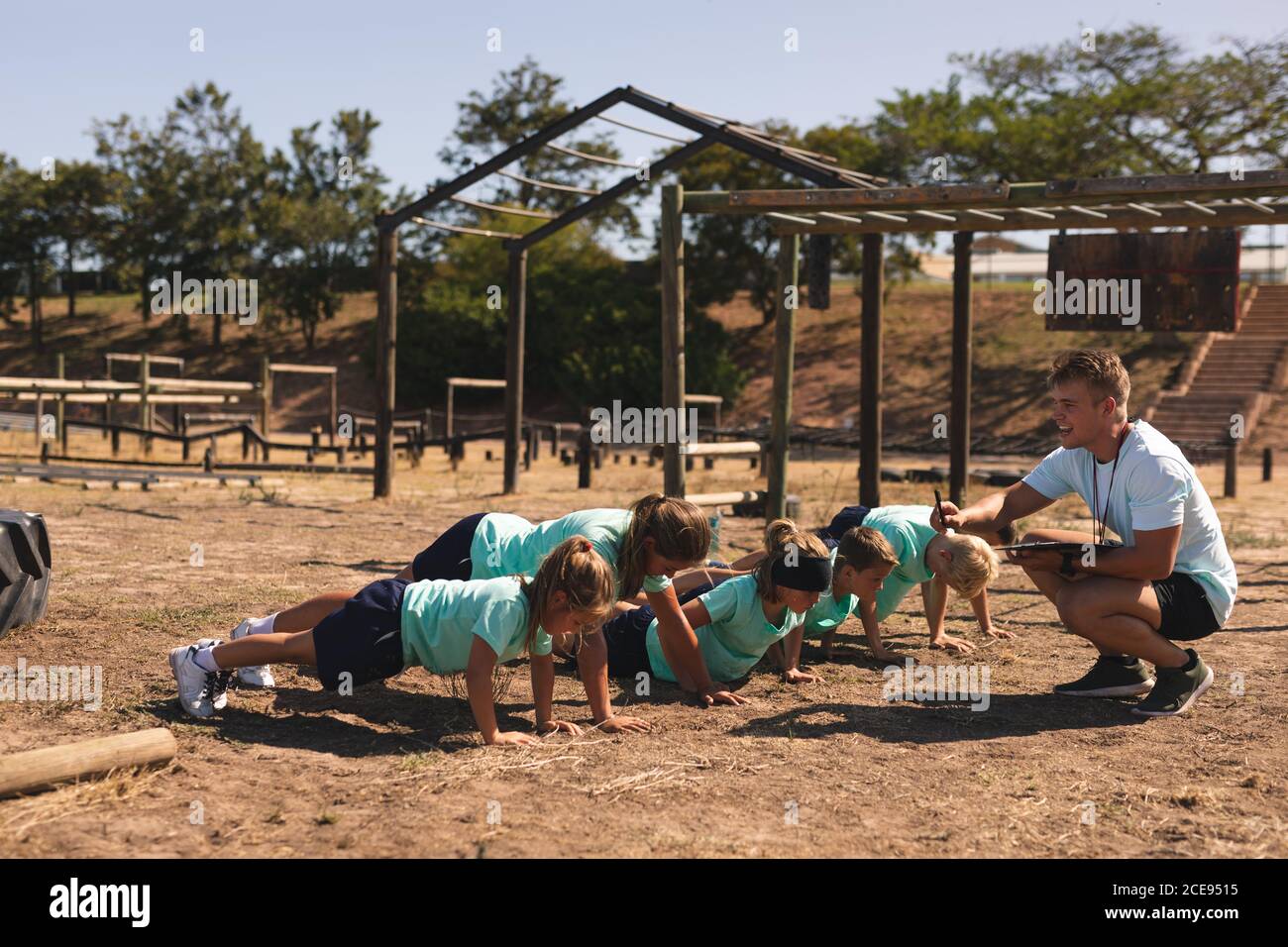 Male fitness coach instructing while kids performing push ups at a boot ...