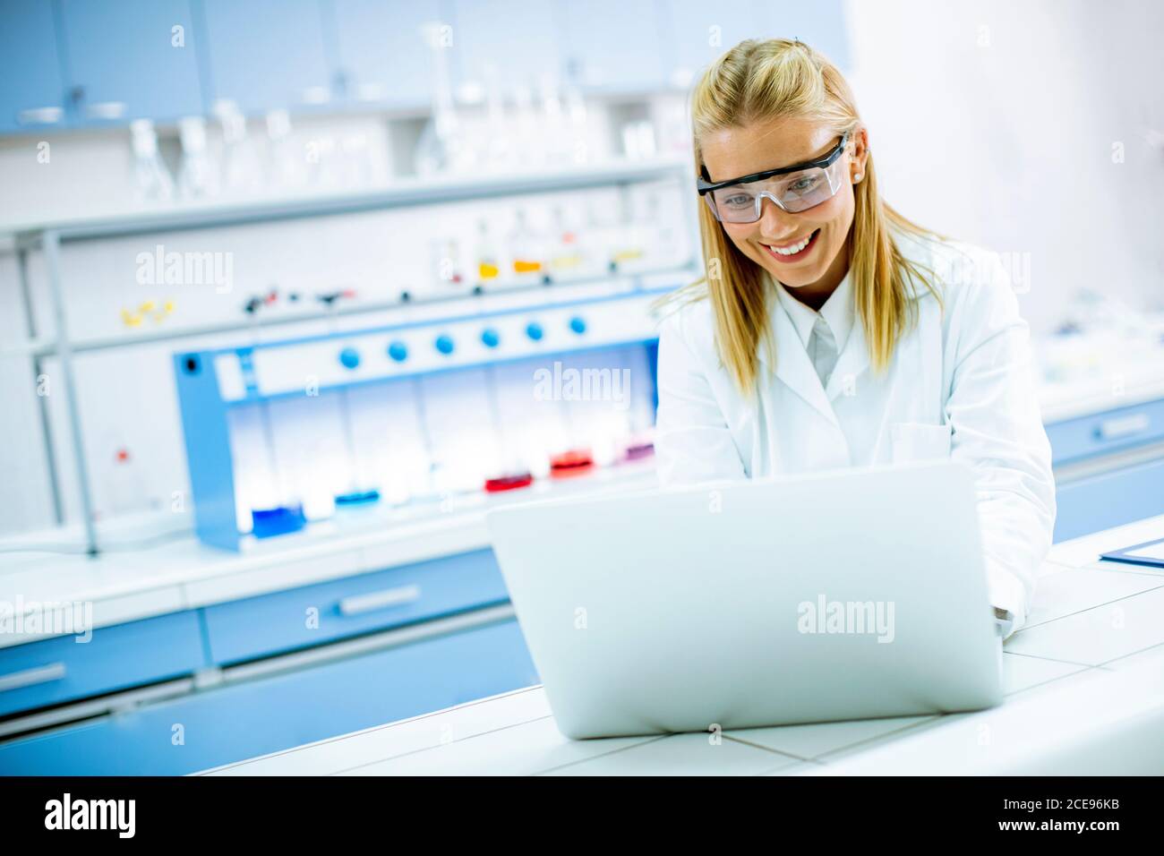 Cute female researcher in white lab coat and protective goggles using ...