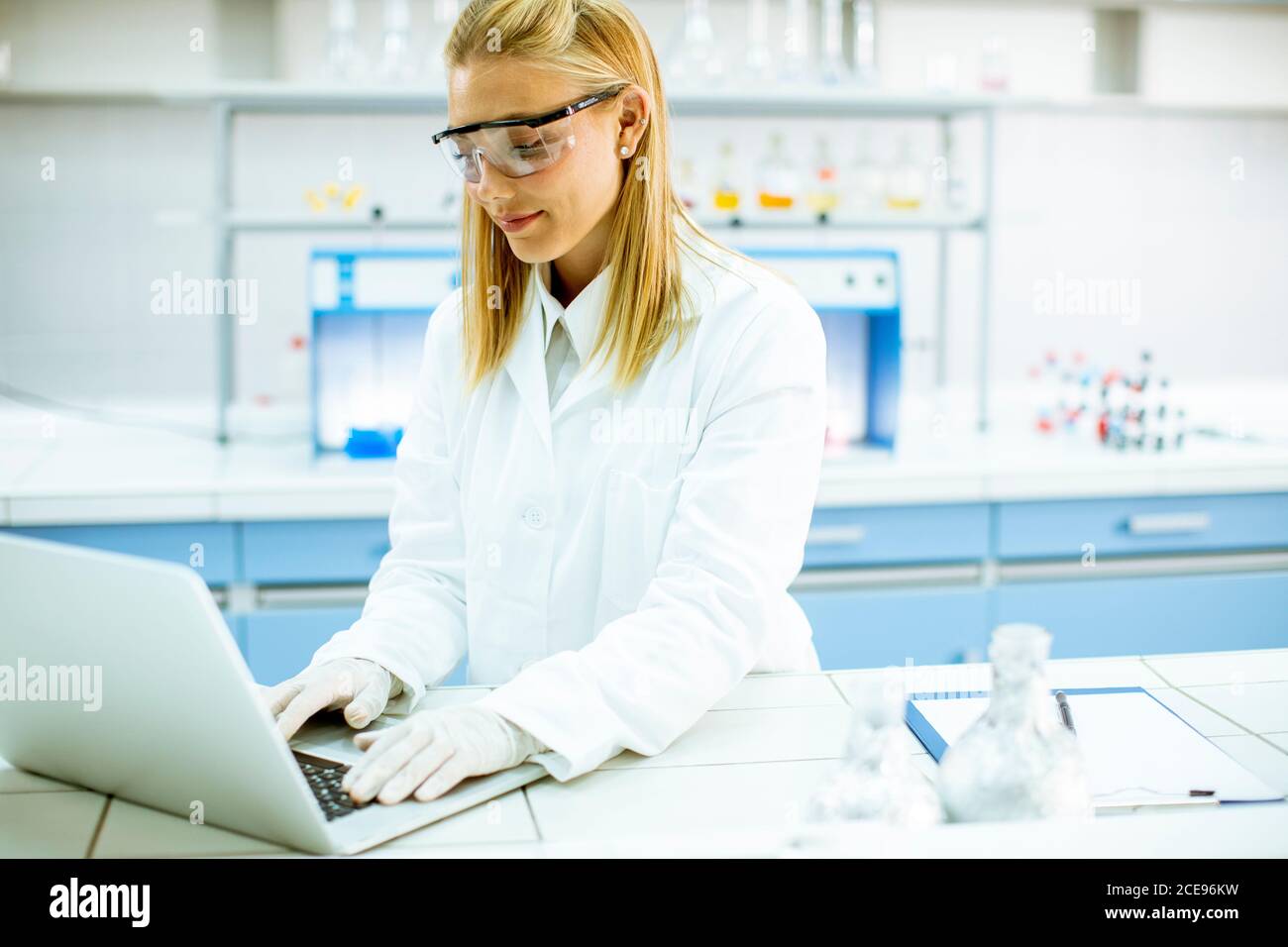 Cute female researcher in white lab coat and protective goggles using ...
