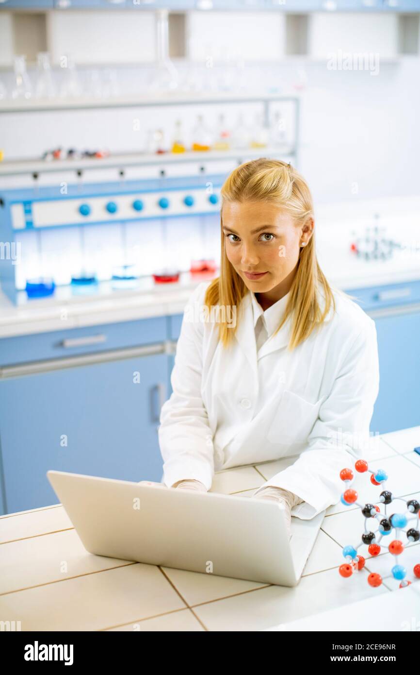 Cute female researcher in white lab coat using laptop while working in ...