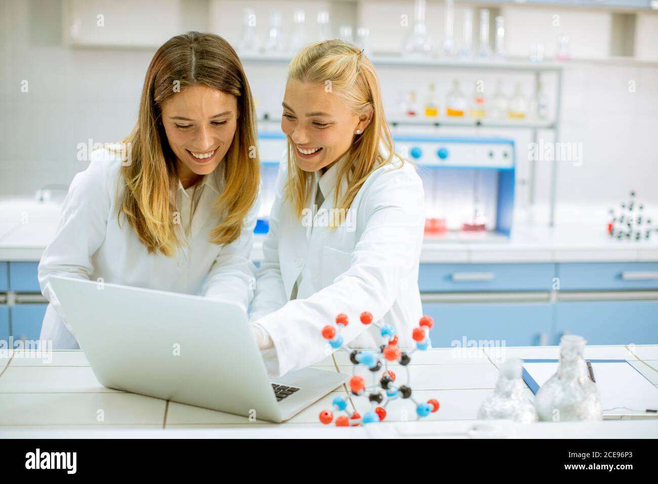 Cute female researchers in white lab coat using laptop while working in ...