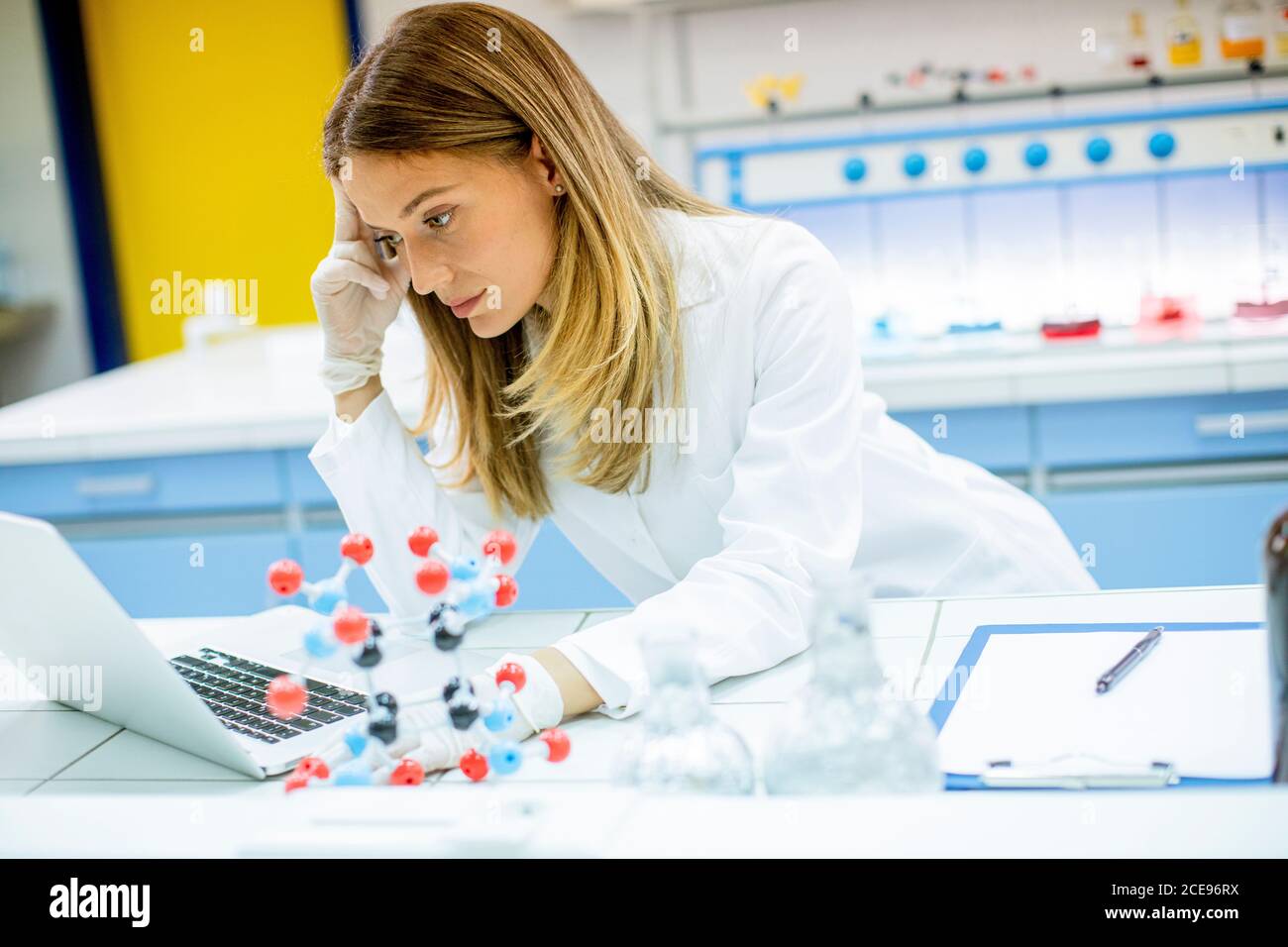 Cute female researcher in white lab coat using laptop while working in ...