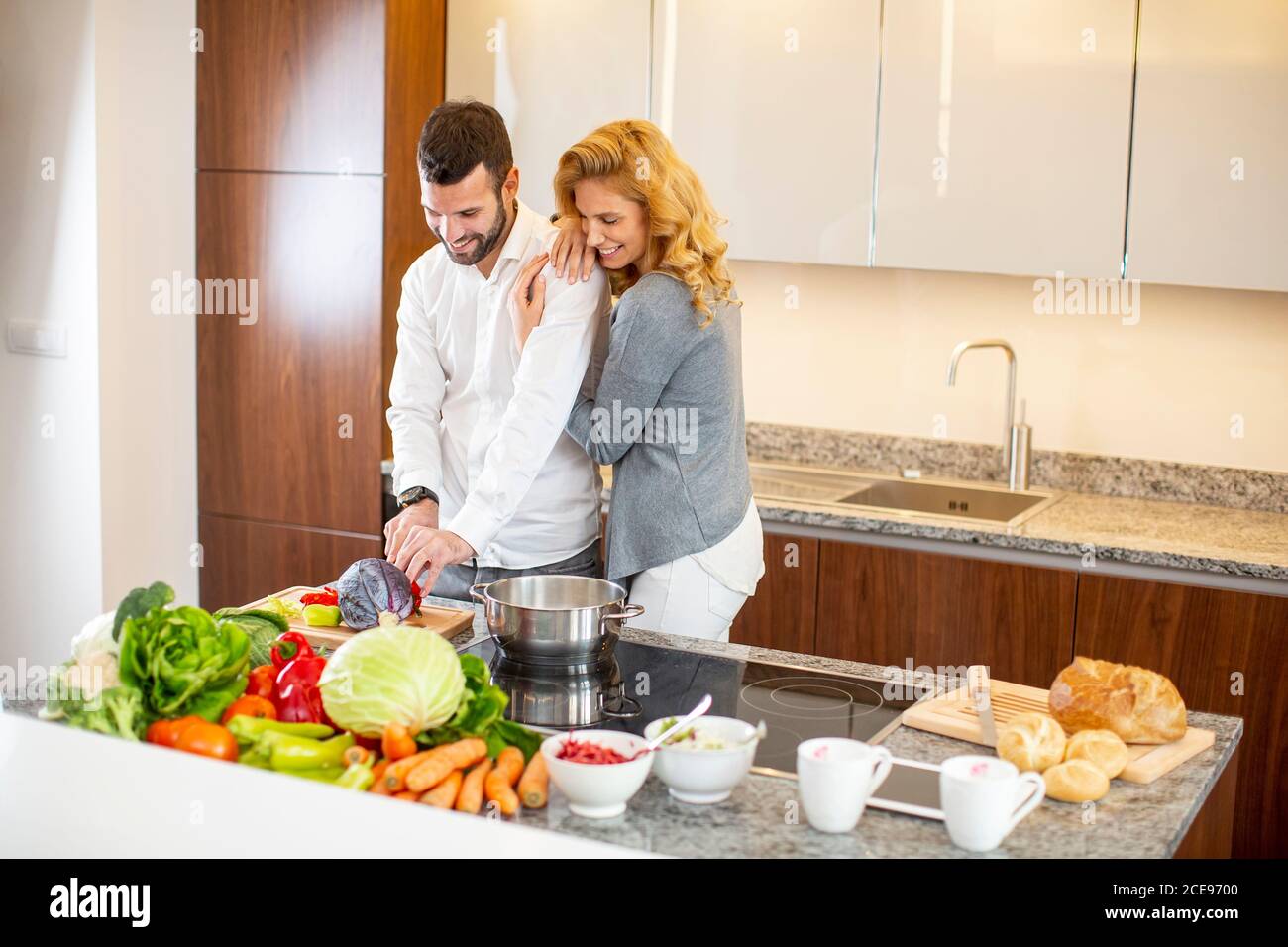 View at young man helping his girlfriend cooking in modern kitchen ...