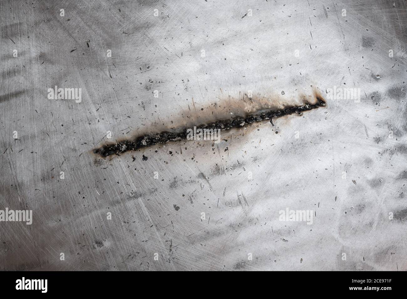 A black straight weld seam on a shiny silver metal plate with traces of ...