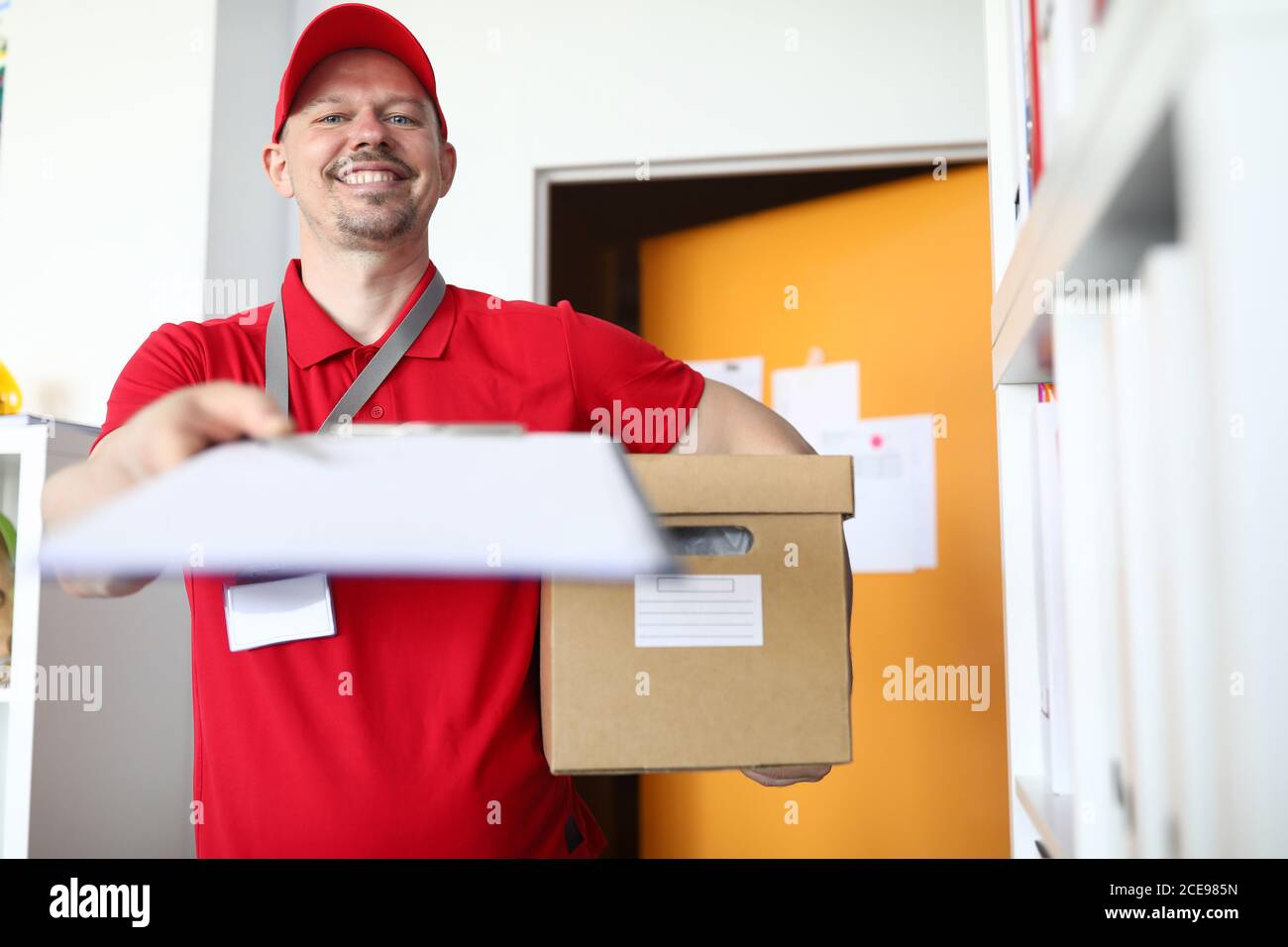 Guy courier in uniform holds parcel and document Stock Photo - Alamy