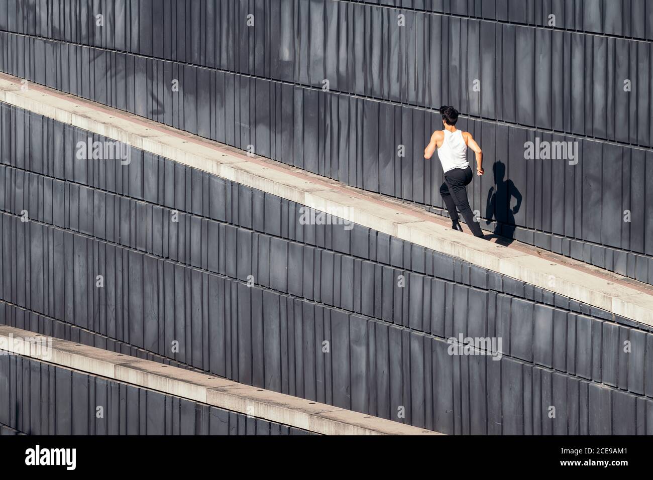 rear view of sporty man running fast up a ramp in a concrete jungle ...