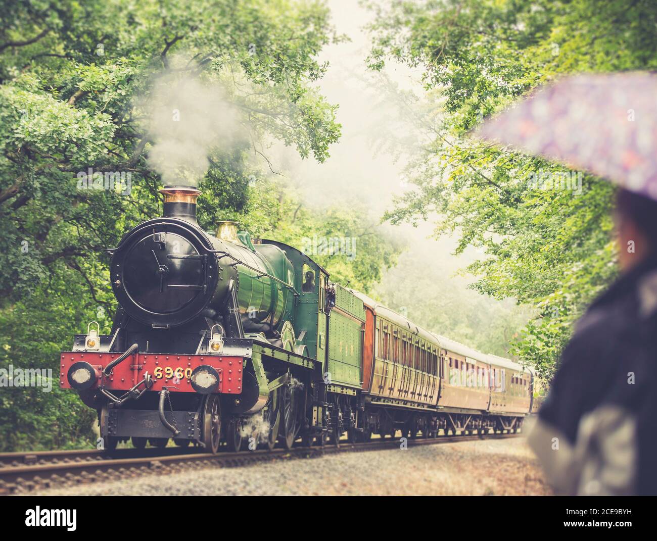 Woman with umbrella watching approaching vintage steam train passing in ...