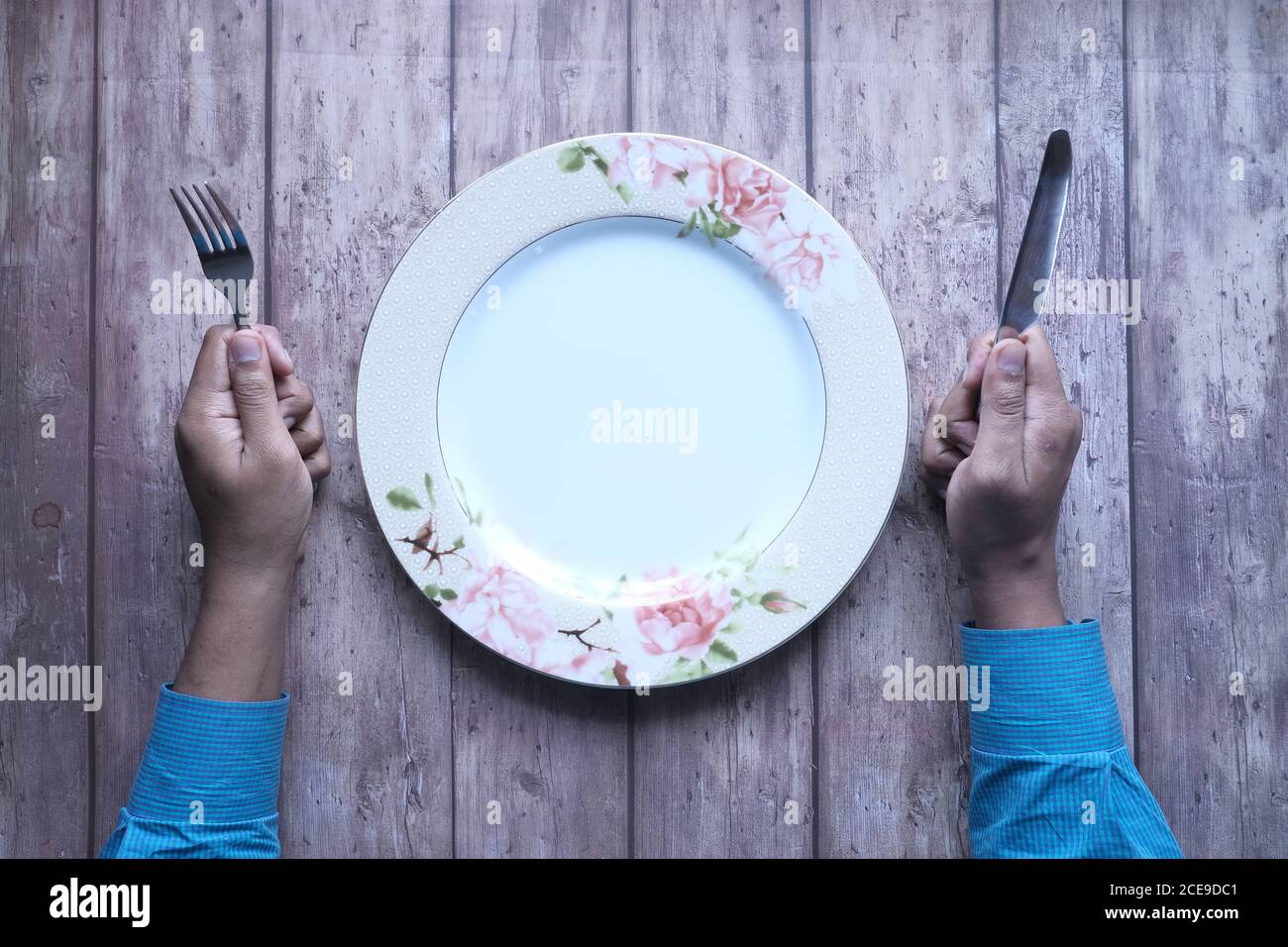 hand holding cutlery and empty plate on wooden background top down ...