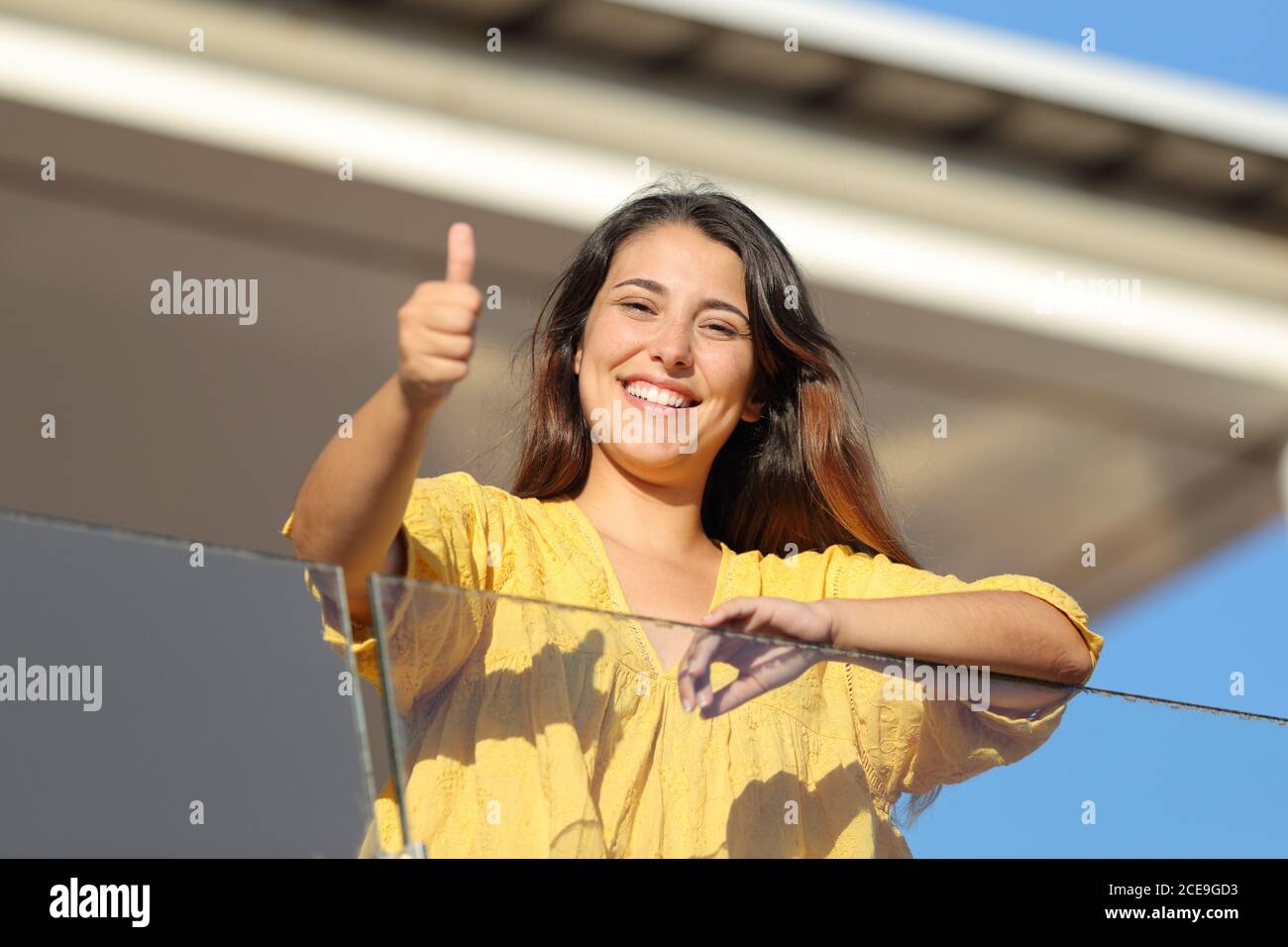 Happy apartment renter with thums up looks at you in a balcony a sunny ...