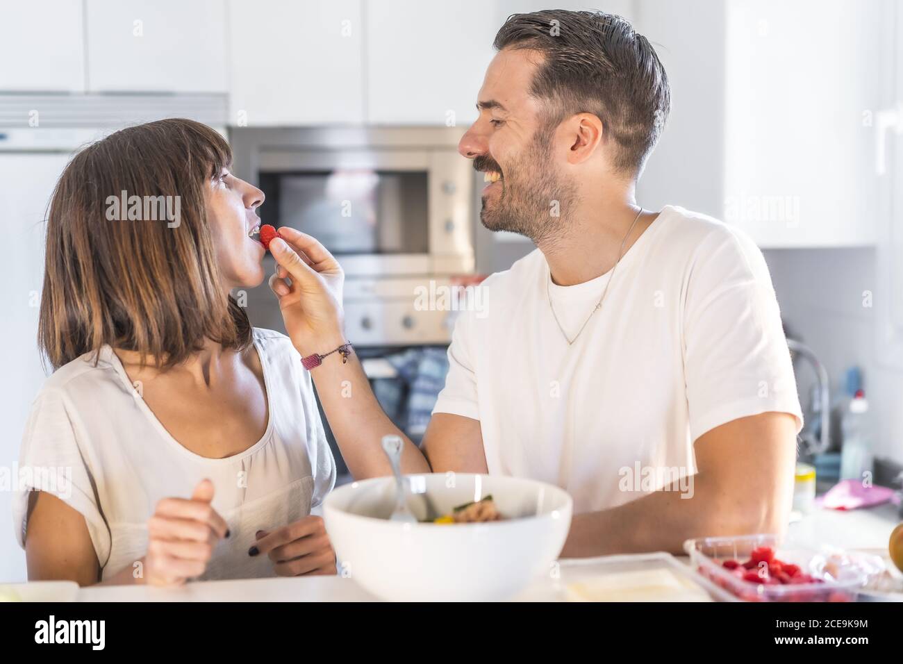 Caucasian male giving a raspberry to his wife while cooking at the ...