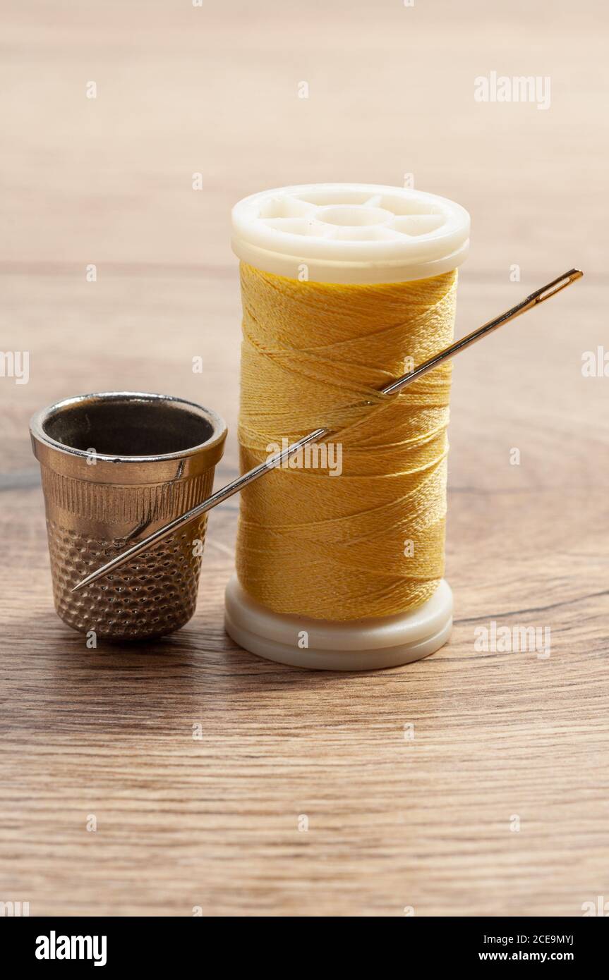 Vertical closeup shot of a roll of yellow thread with a needle and a ...