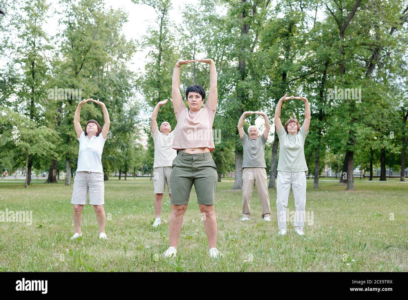 Group of senior people and their coach raising arms up while stretching ...