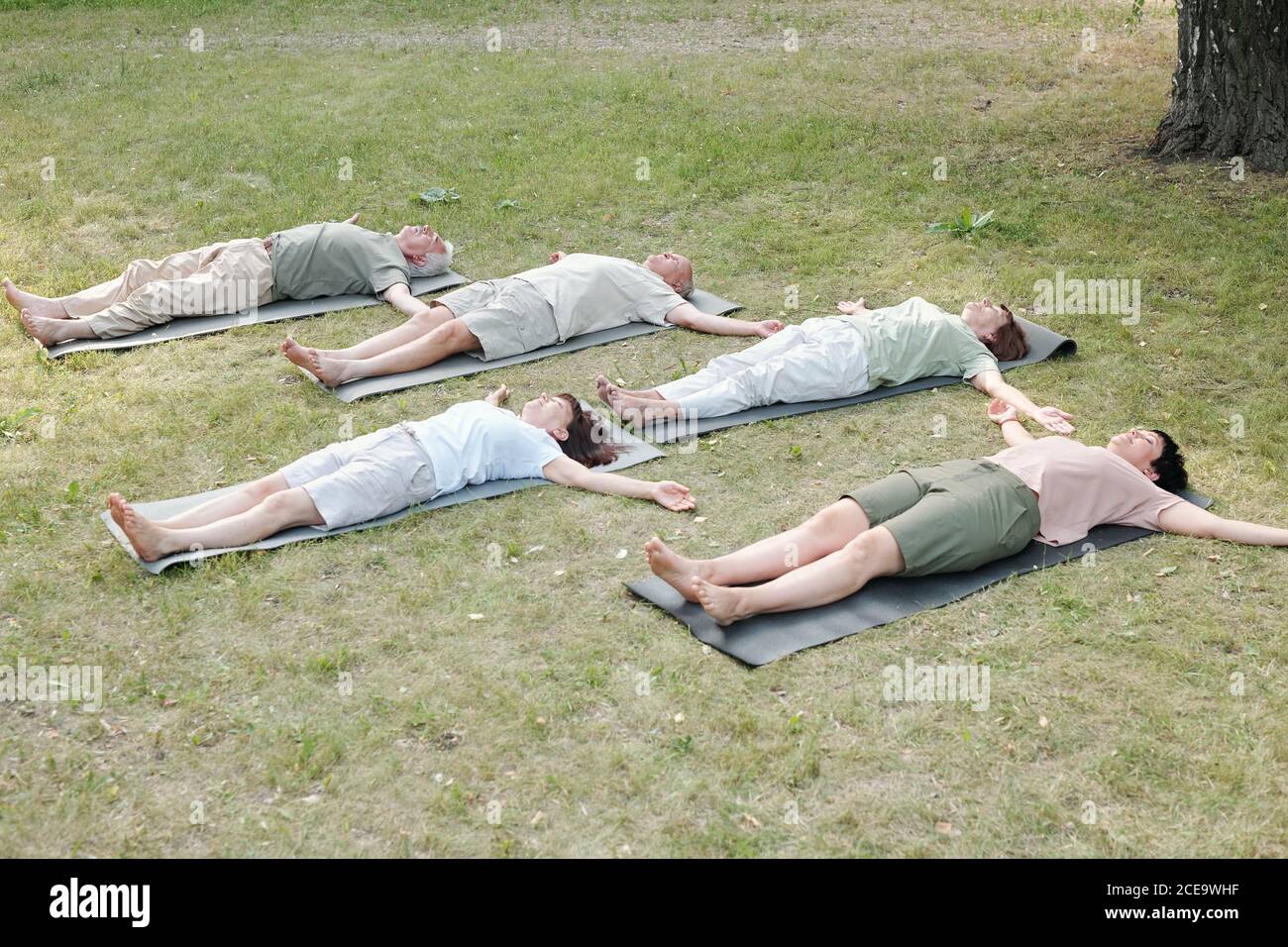 Group of mature yoga students lying in corpse pose on mats while ...