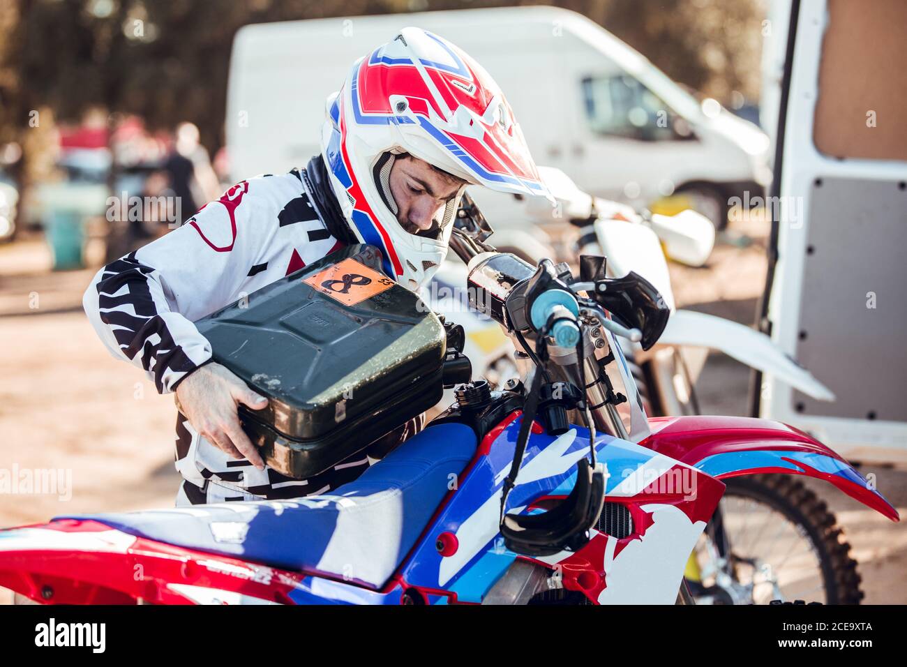man in helmet and racer uniform filling motorcycle with fuel before ...
