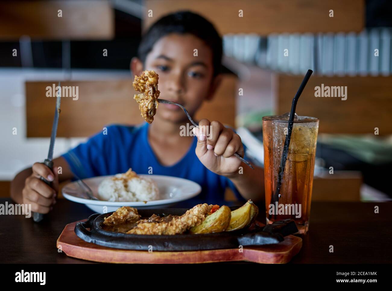 Cute boy eating grilled Chicken steak on stoned plate in restaurant ...