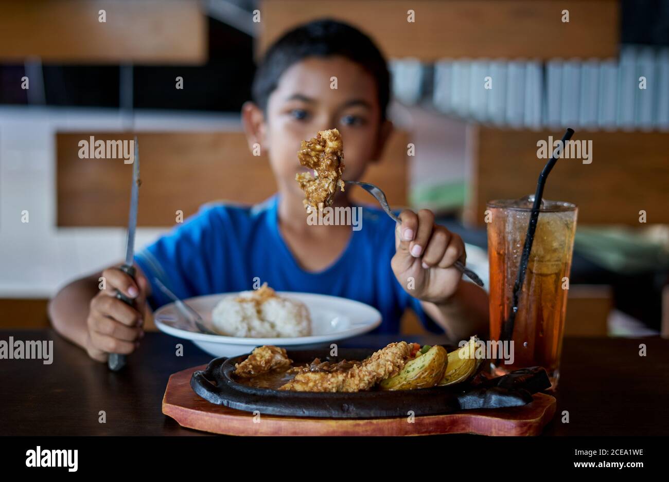 Cute boy eating grilled Chicken steak on stoned plate in restaurant ...