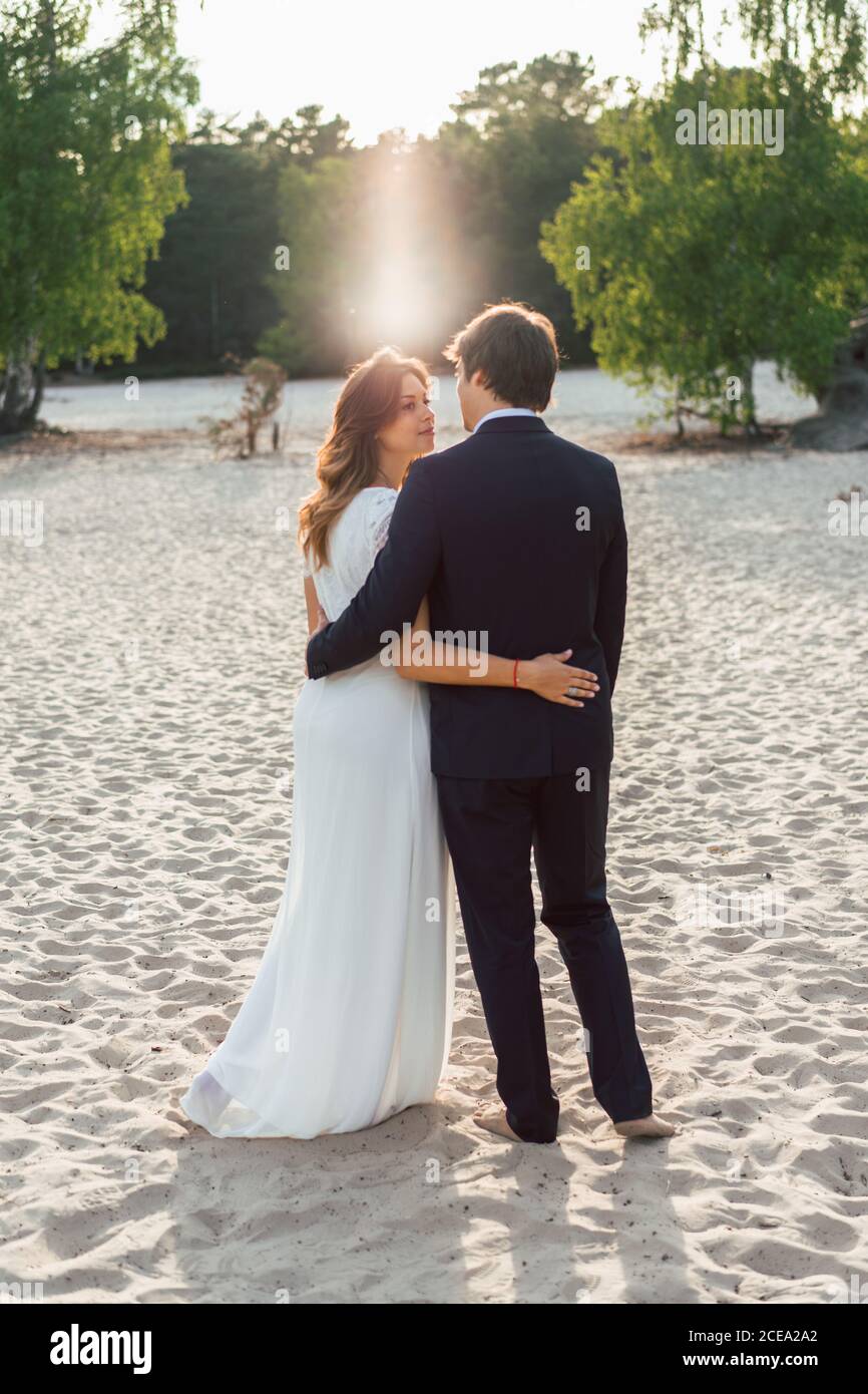 Loving man embracing beautiful bride in elegant dress and looking at ...