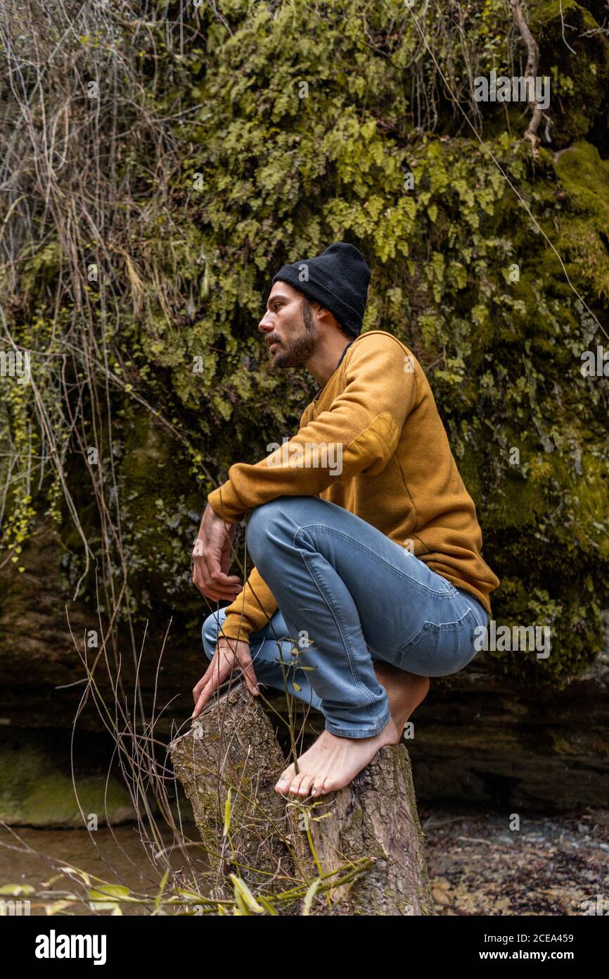 Side view of handsome barefoot male in casual outfit looking away while ...