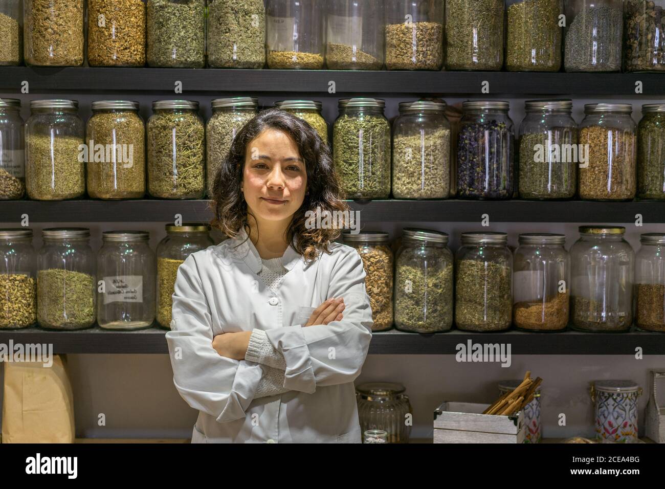 Pretty shop assistant Woman standing with arms crossed at shelves with ...