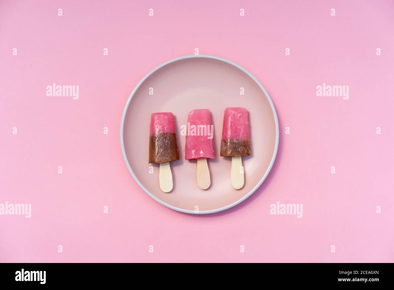 Colorful pink and brown popsicles lying in row on pastel plate on pink ...