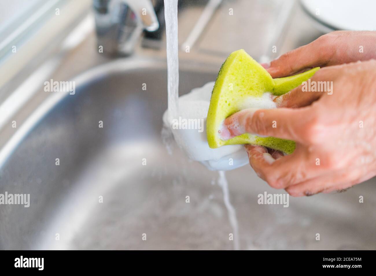 Crop hands of unrecognizable person washing cup with sponge in sink on ...
