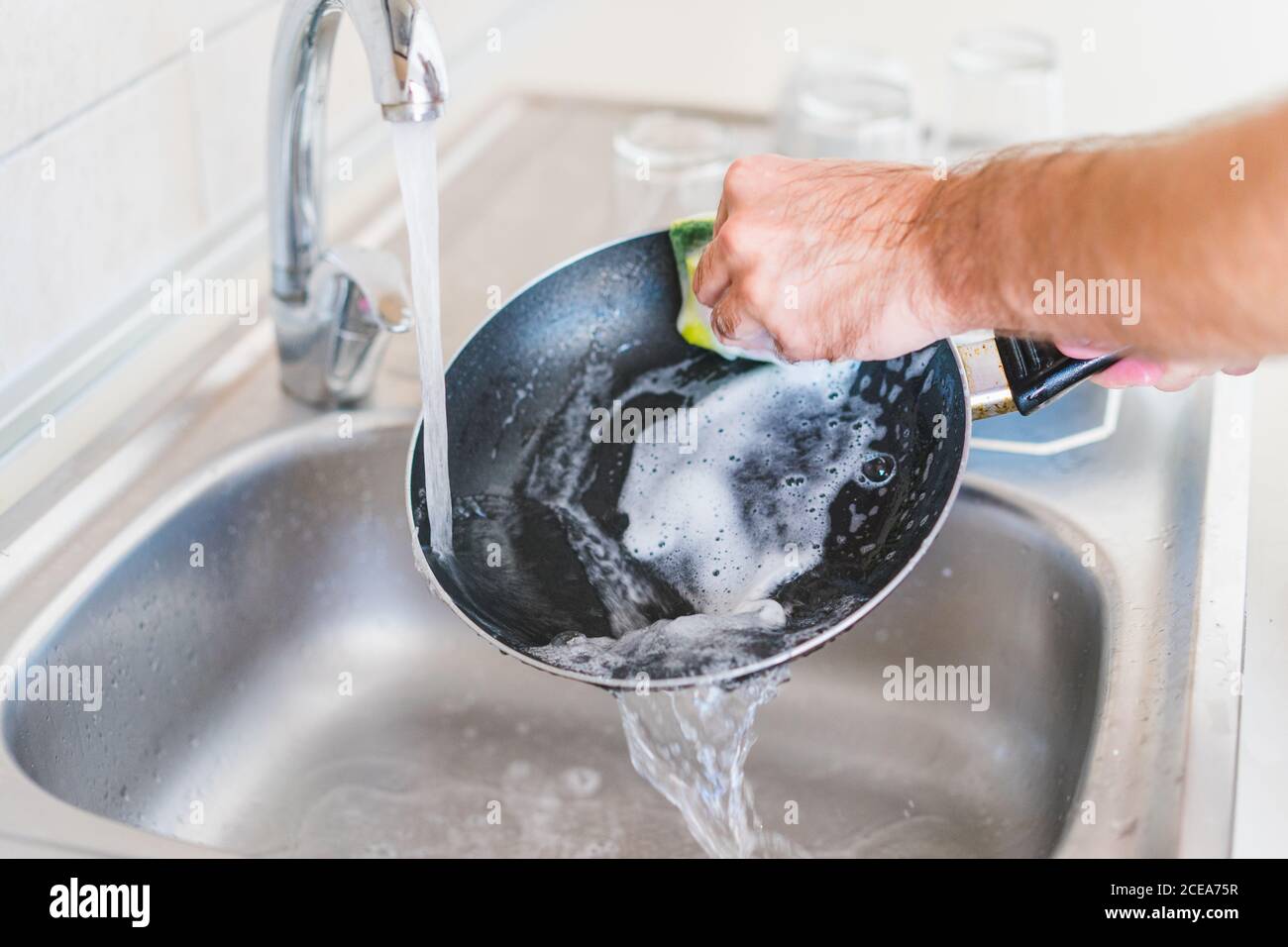 Hands of unrecognizable person washing frying pan in sink on kitchen ...