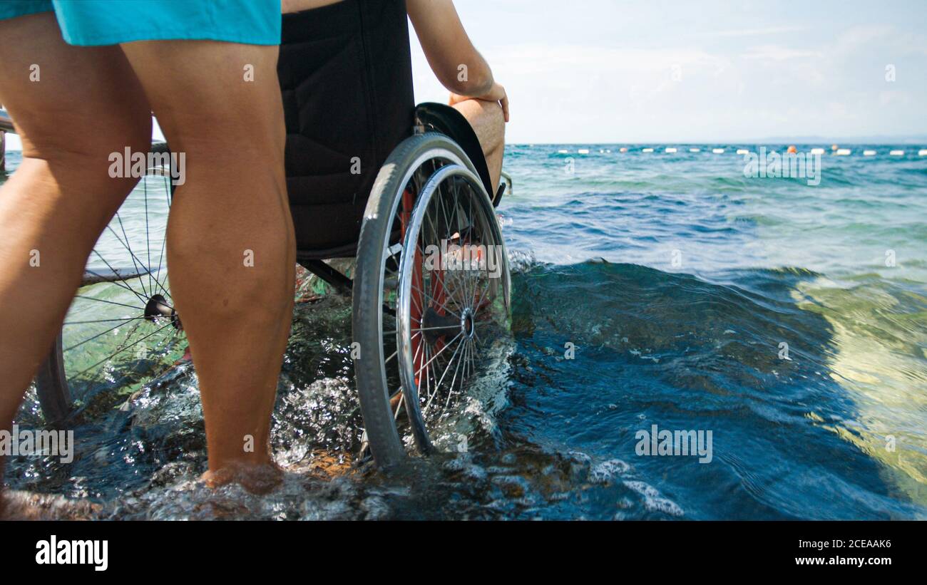 Disabled man at beach swimming on a wheelchair with assistance help on ...