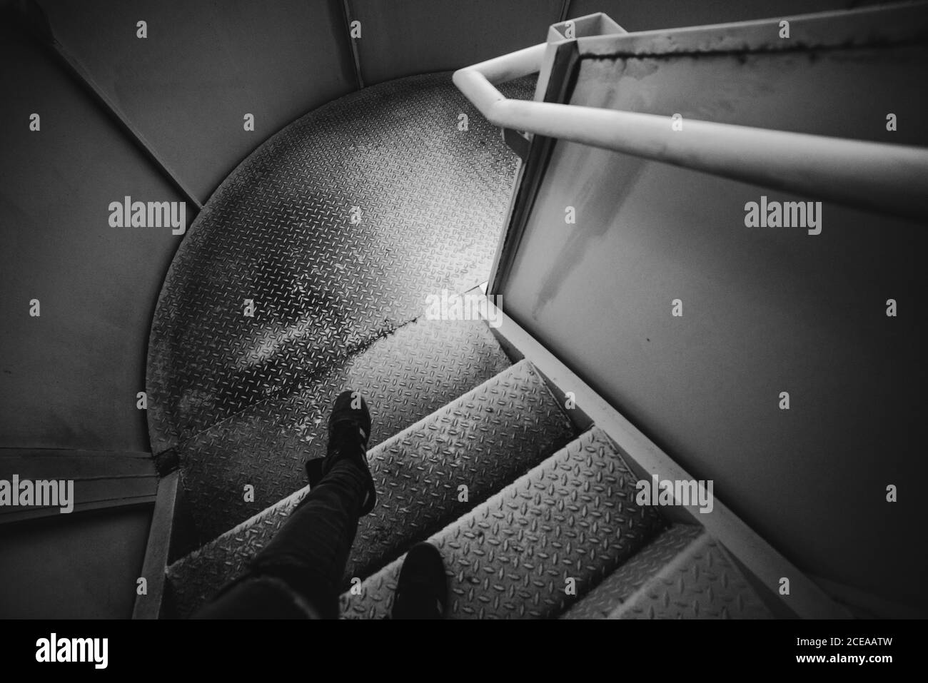 Legs of anonymous person standing on metal spiral stairway inside jail ...