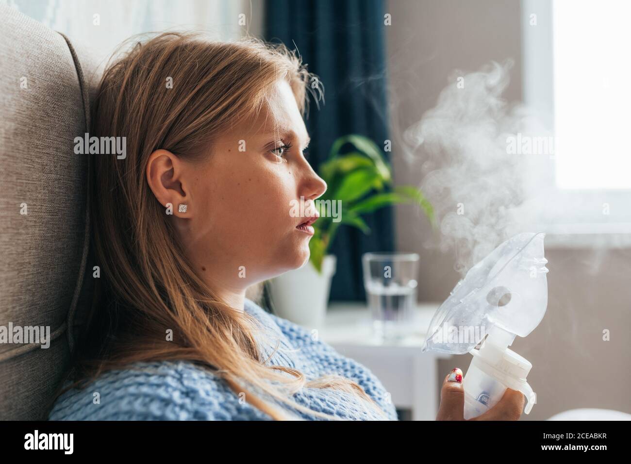 Portrait of a young blonde woman do inhalation with steam nebulizer at ...