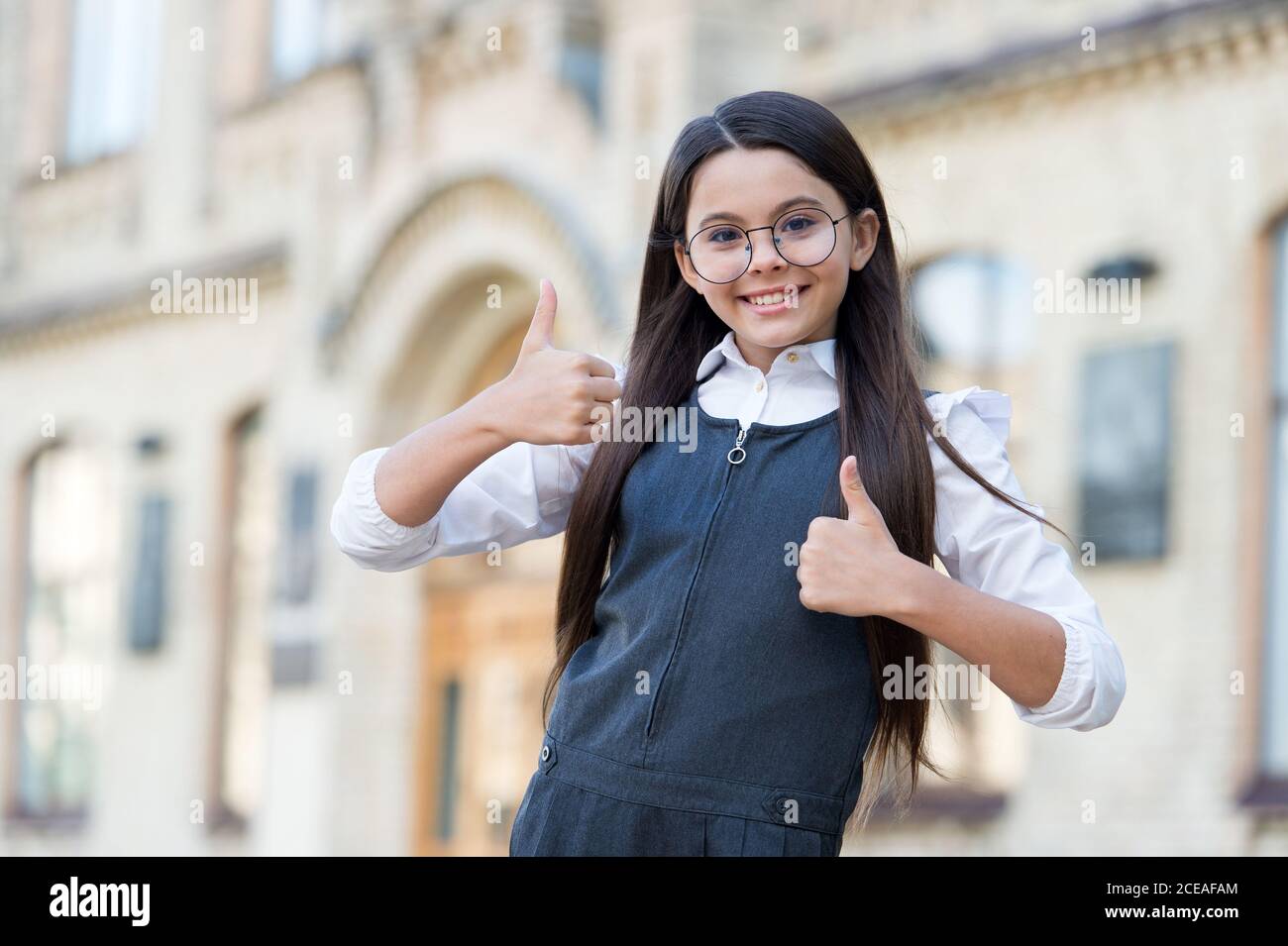 Happy child in school uniform give thumbs ups hand gesture in ...