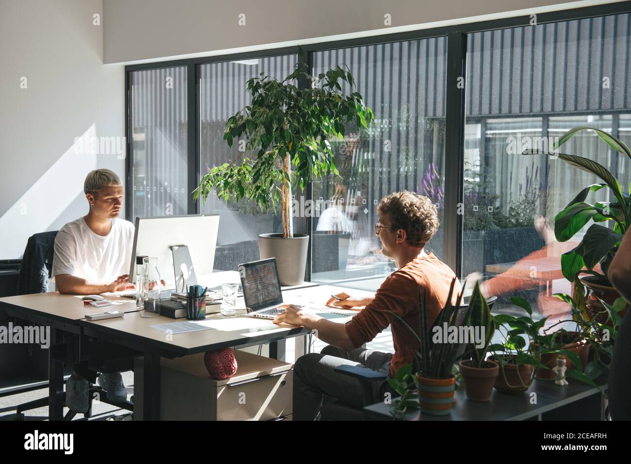 Men sitting at tables in front of each other inside of open space ...