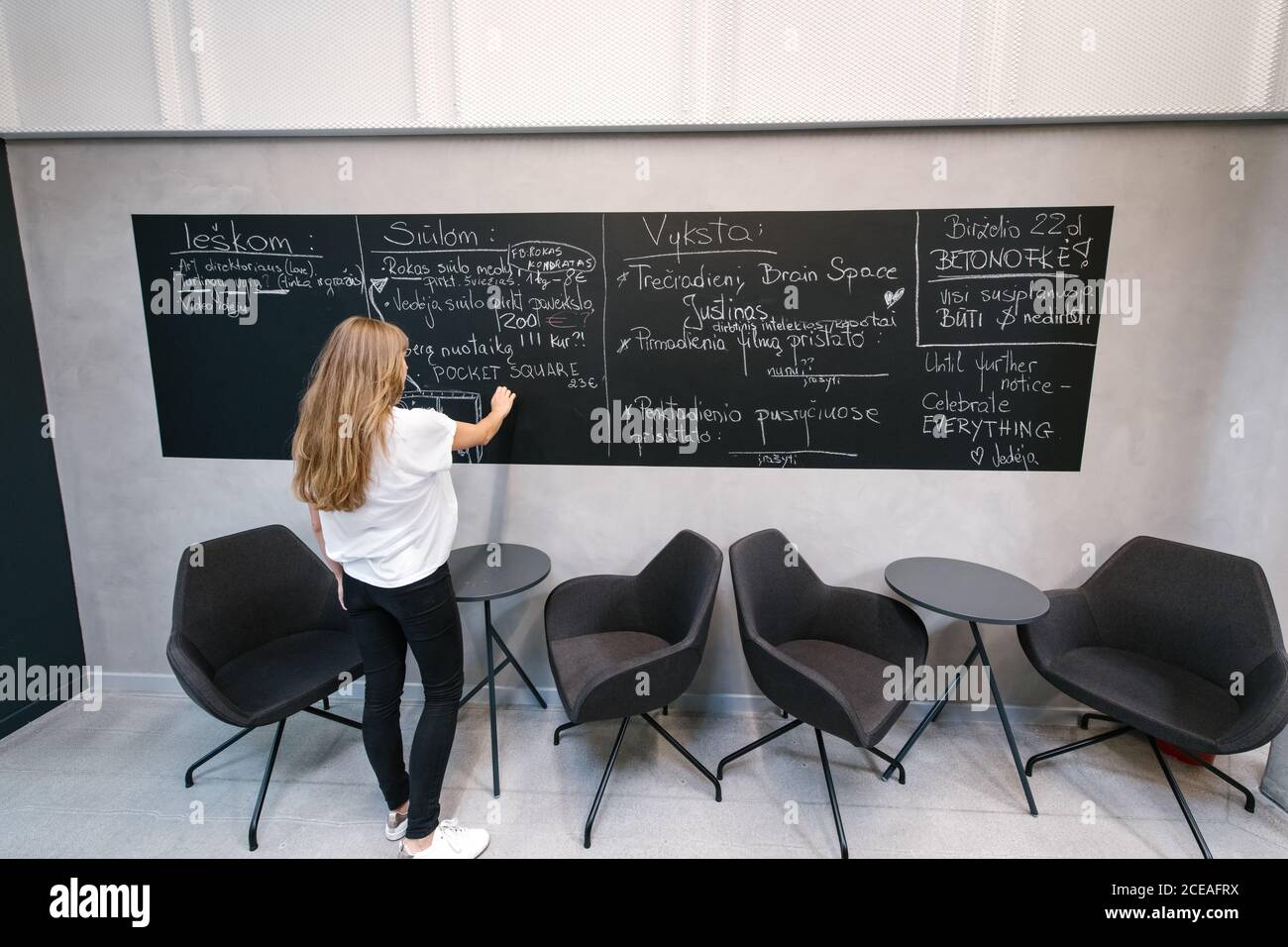 Back view of casual Woman writing on blackboard in hall of modern ...