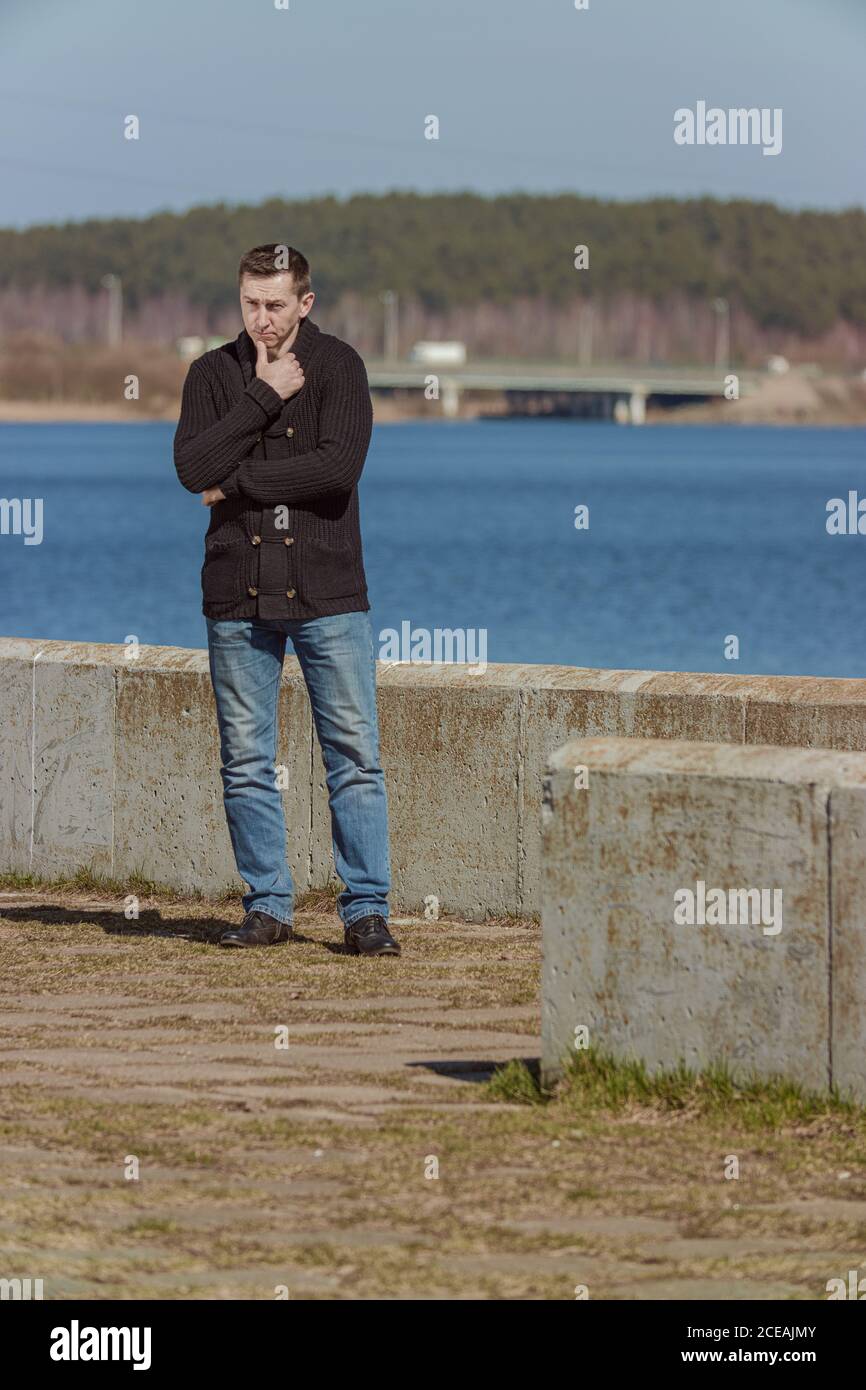 A young adult man in a black knitted jacket and jeans stands on the ...