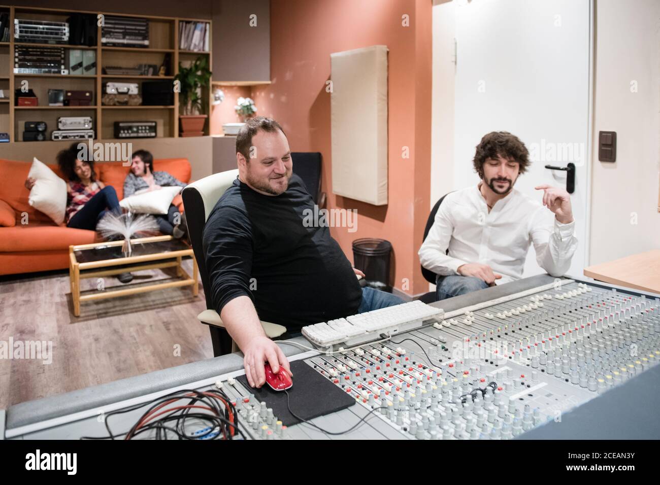 Two sound directors sitting at audio mixer board while working in ...