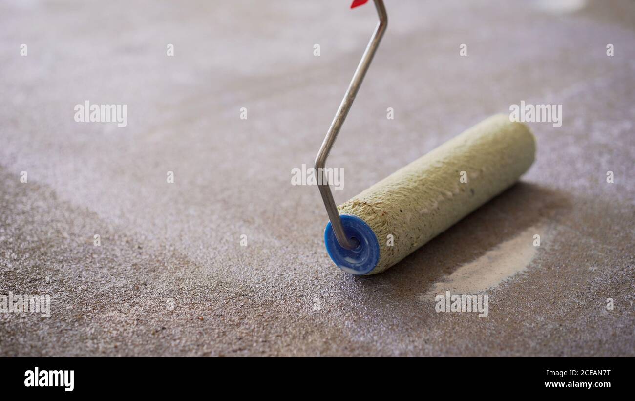 A worker applies the primer to the concrete floor with a roller ...