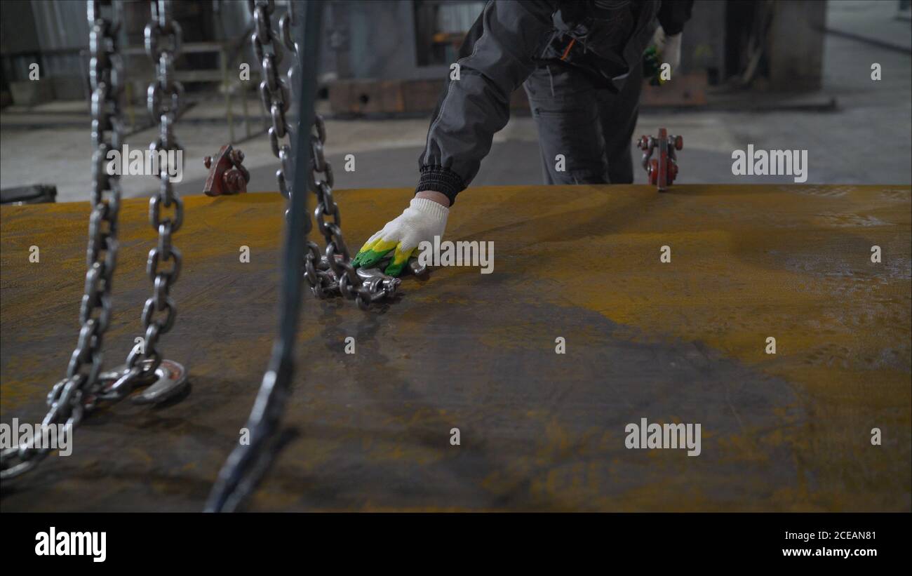 A worker hooks a metal sheet to a crane. Crane chain and hook at an ...