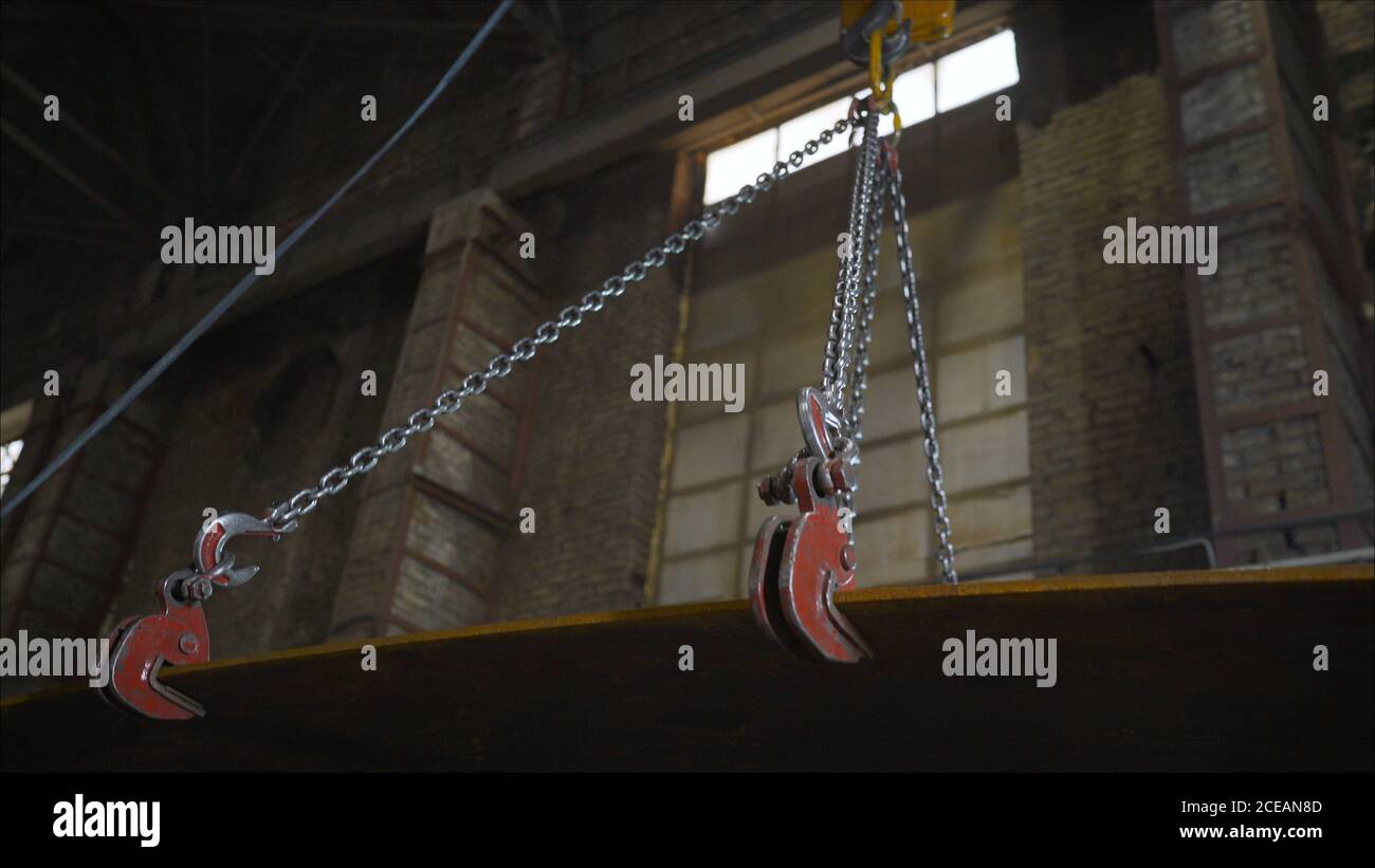 A worker hooks a metal sheet to a crane. Crane chain and hook at an ...