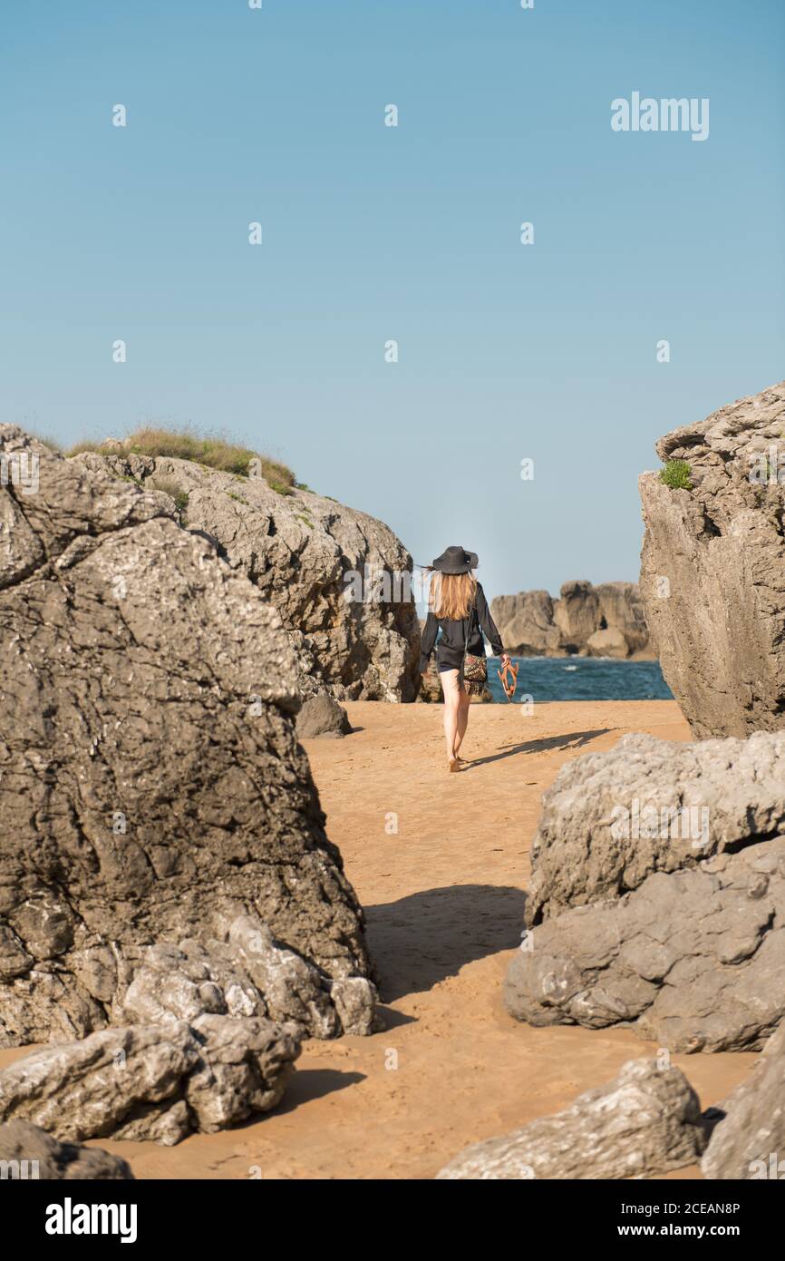 Back view of anonymous lady walking on sandy shore amidst boulders ...
