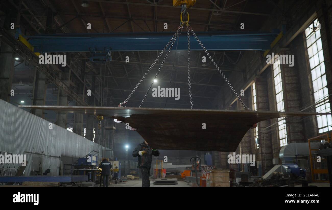 A worker hooks a metal sheet to a crane. Crane chain and hook at an ...
