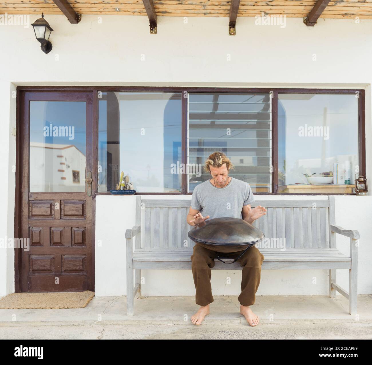 Barefooted guy in t-shirt sitting on seat with big hand drum near door ...
