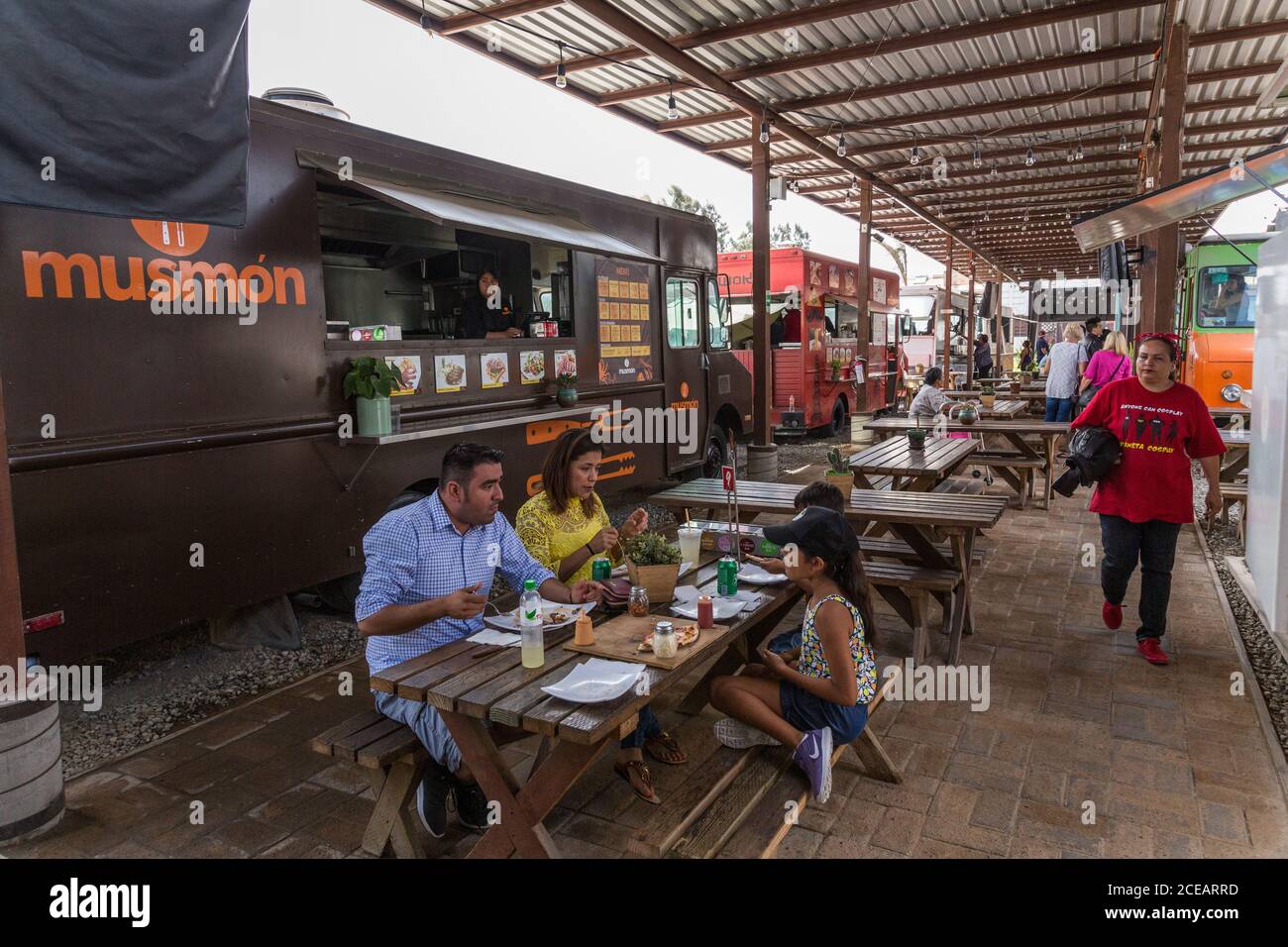 A familiy in an outdoor eating area with mobile food vender's trucks in ...