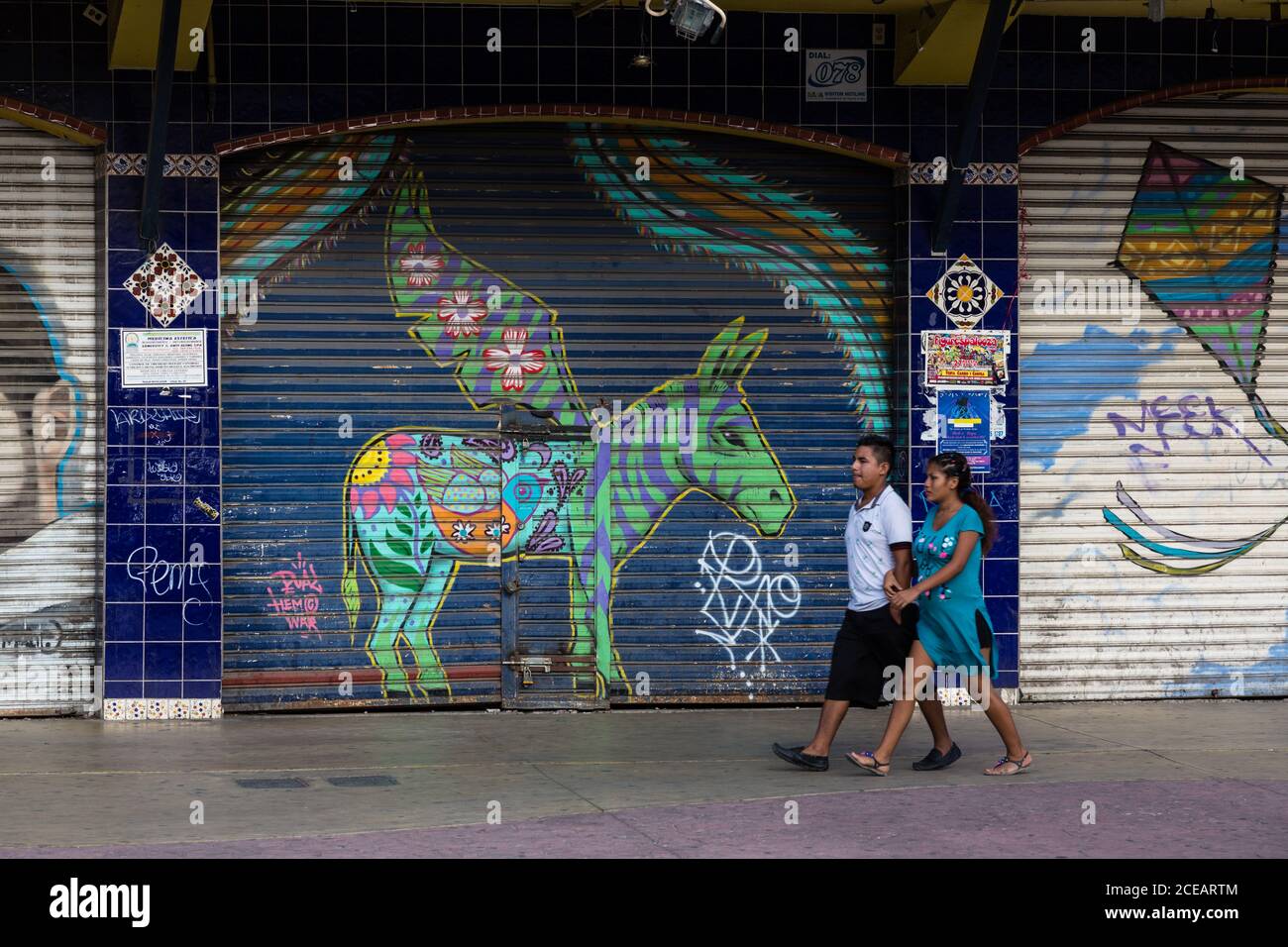 A Mexican couple walks in front of street art on a store-front door ...