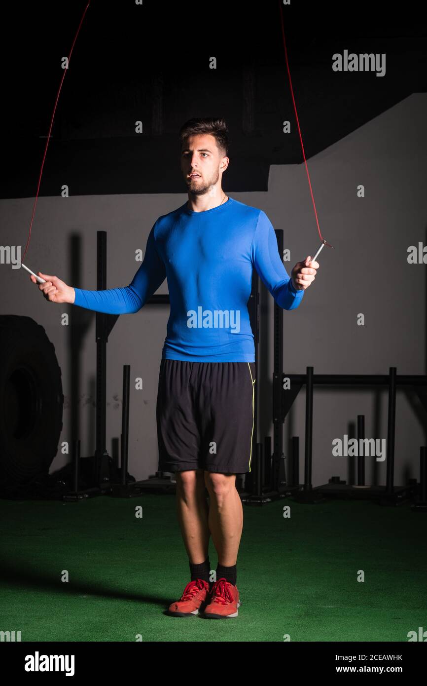 Athletic young concentrated guy in sportswear jumping with skip rope in ...