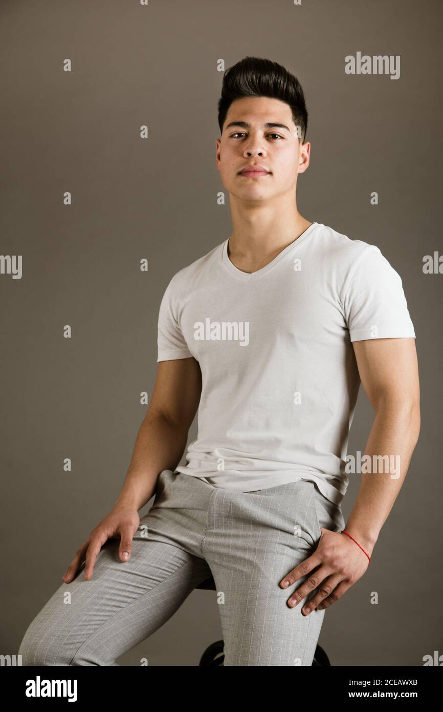 Fit male sitting and posing on high chair looking at camera in studio ...