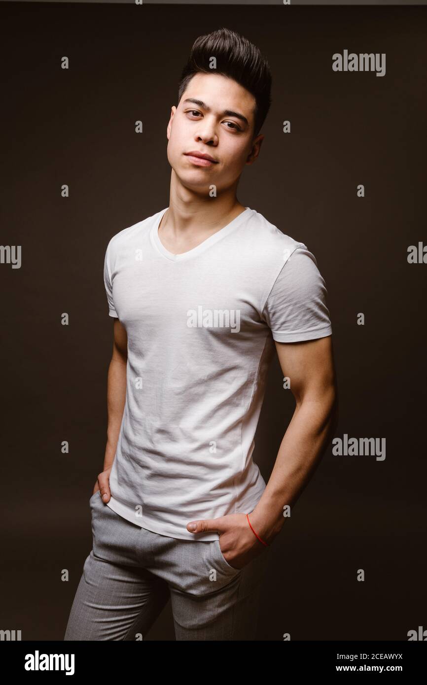 Handsome man in white t-shirt and pants over dark background standing ...